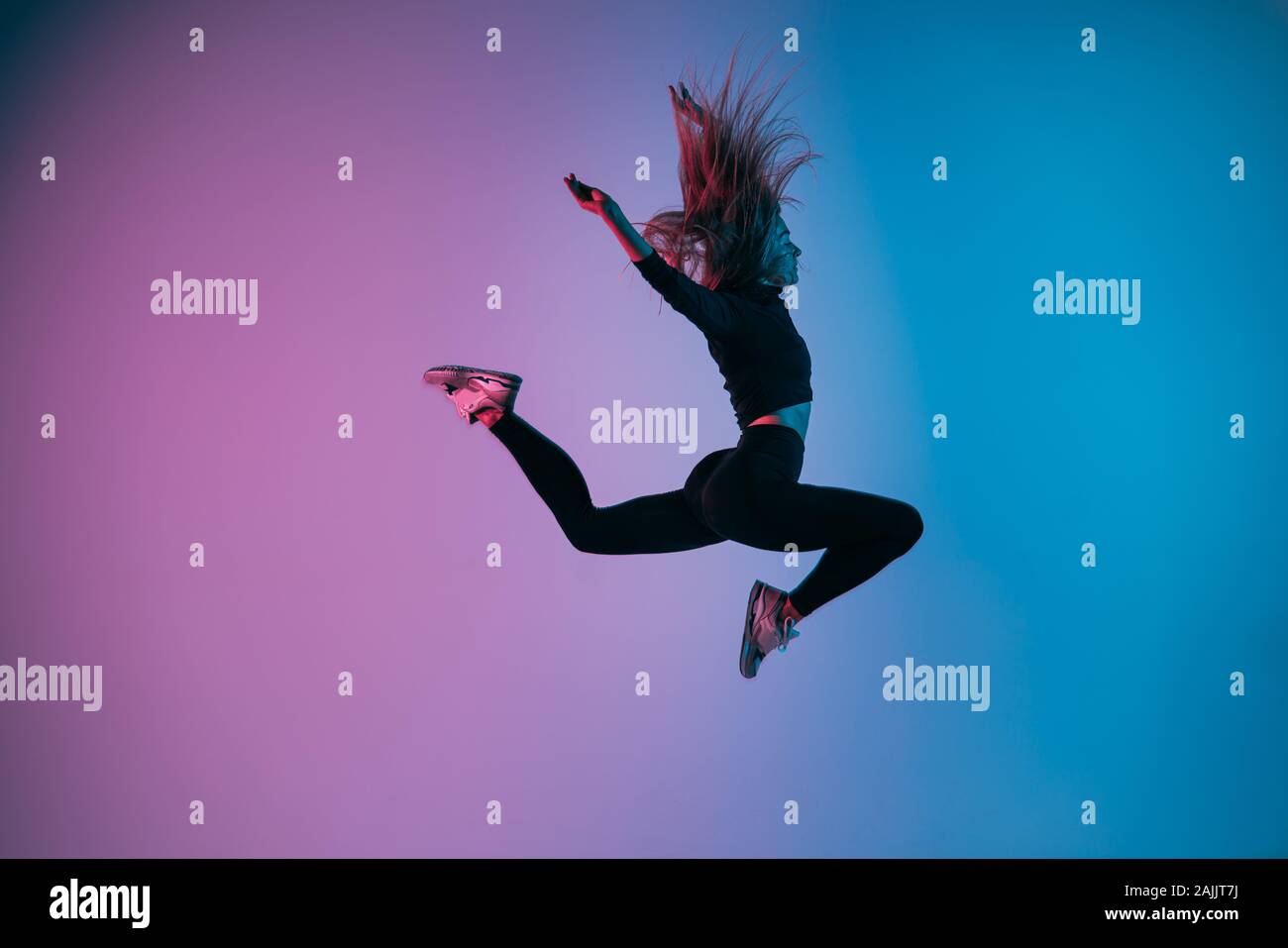 Sporty girl in charismatic jump moment against trendy color background ...