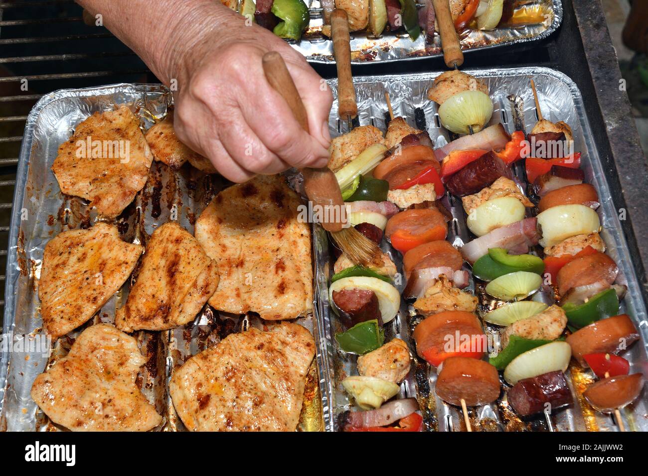 A human puts a spice sauce on meat and vegetables on the grill Stock ...