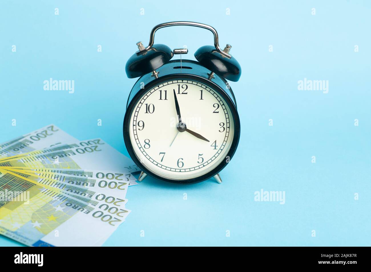 Time and money concept. Euro cash and alarm clock on a blue background ...