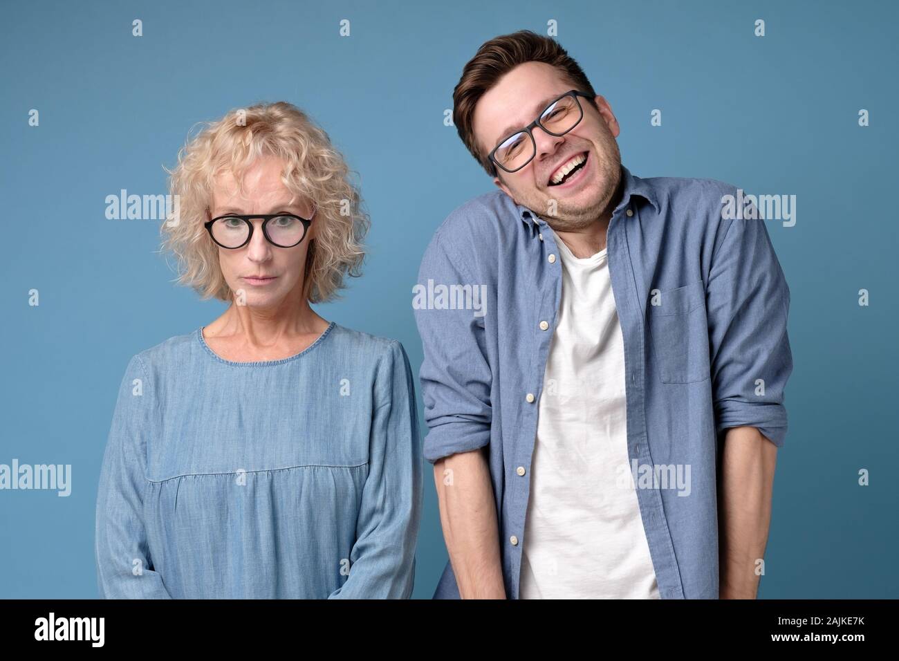 Cheerful handsome man laughing at his annoyed mature coworker, isolated ...