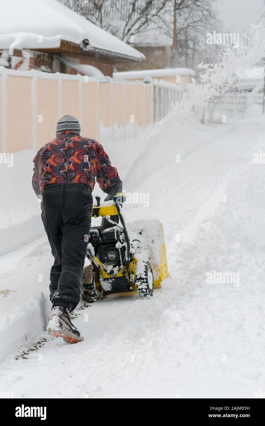 man operating snow blower to remove snow on driveway. Man using a ...
