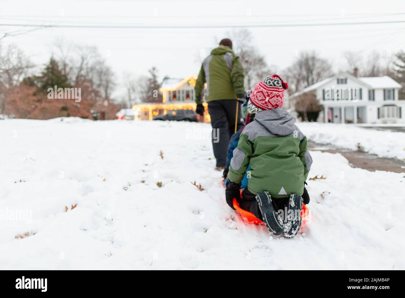 Rear view of father pulling children through the snow on orange sled ...