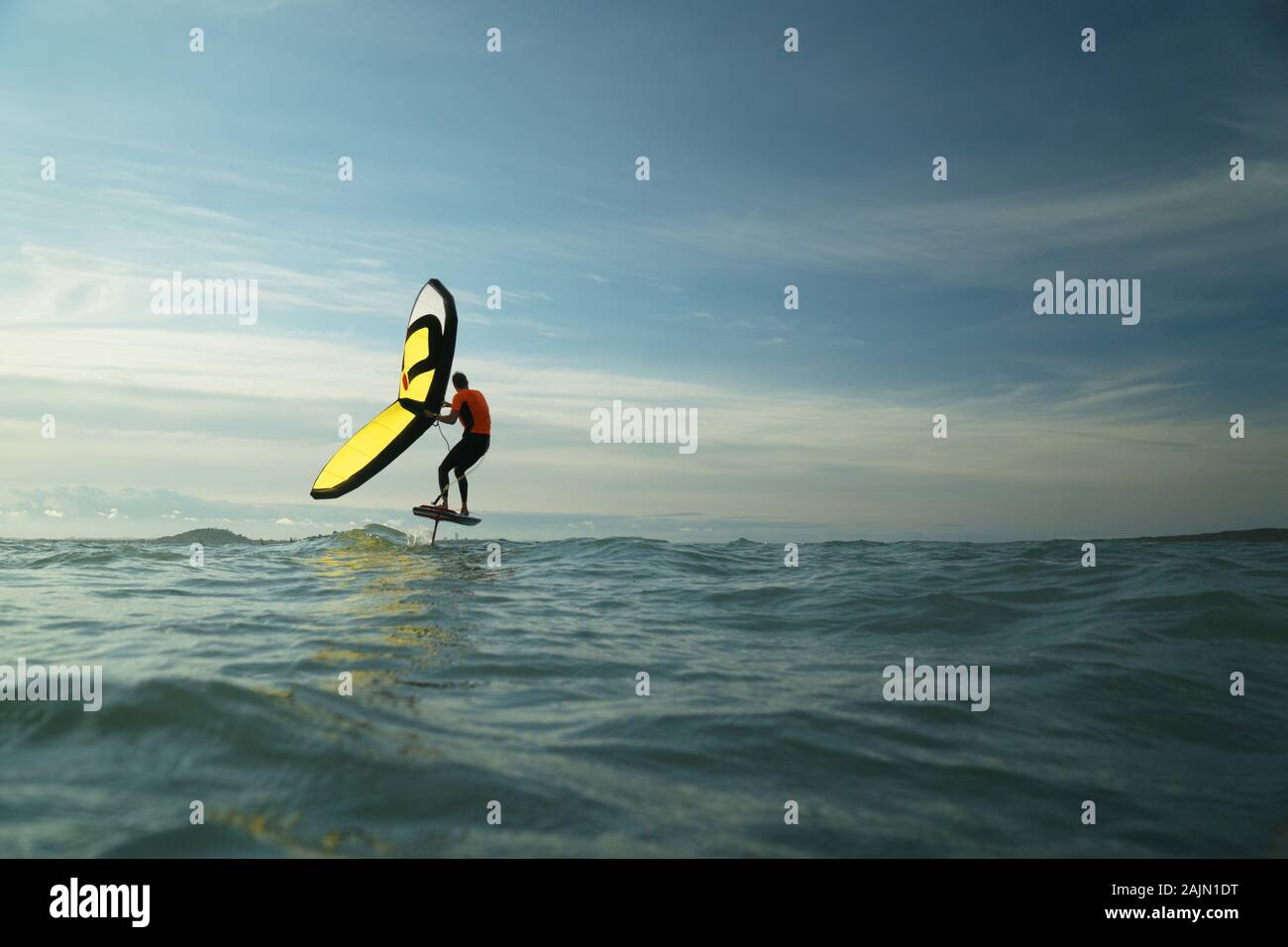 Man riding a hydrofoil surfboard using a hand held foil wing at sea ...