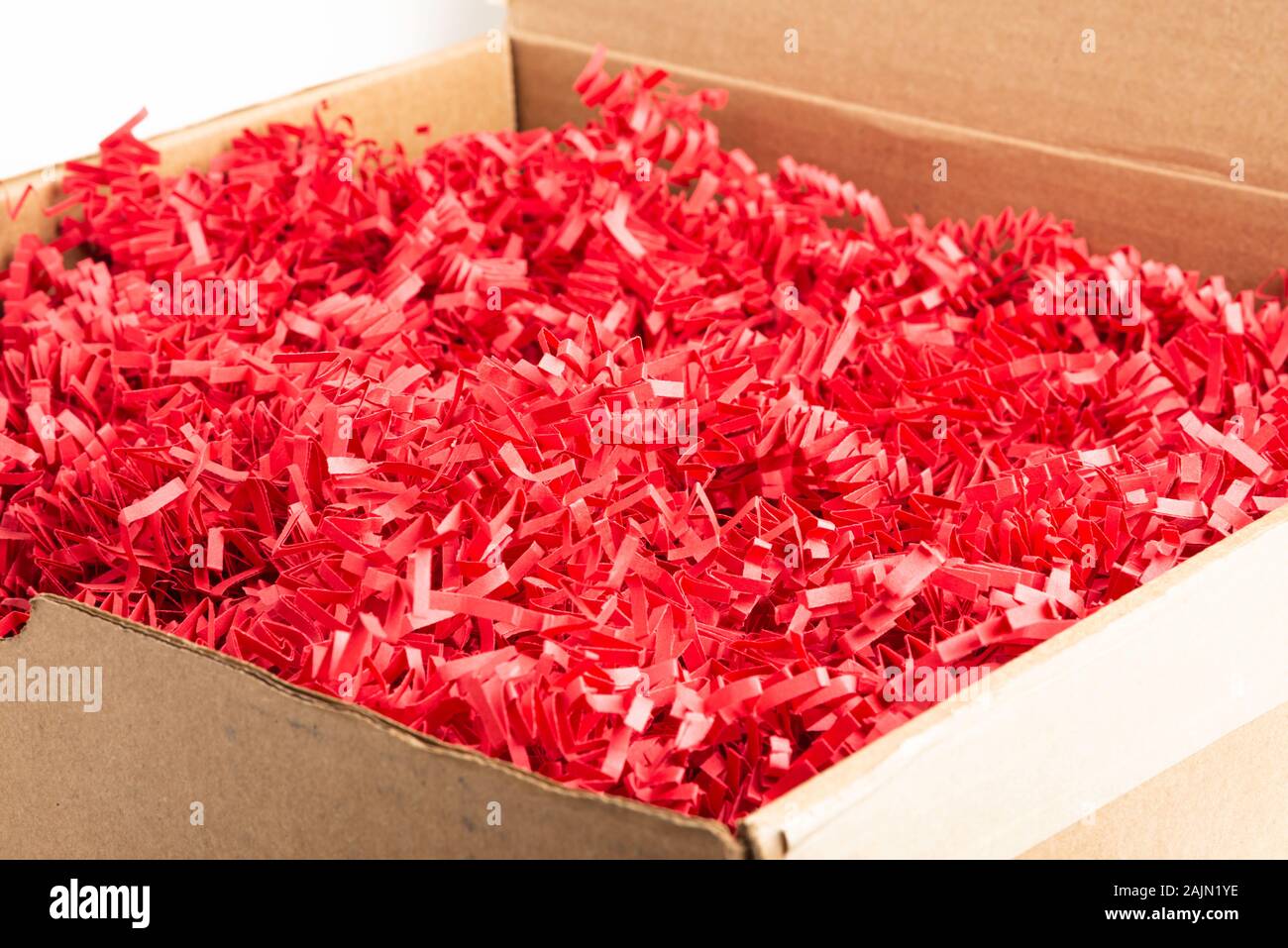 A brown cardboard package box filled with cut and crimped red paper ...