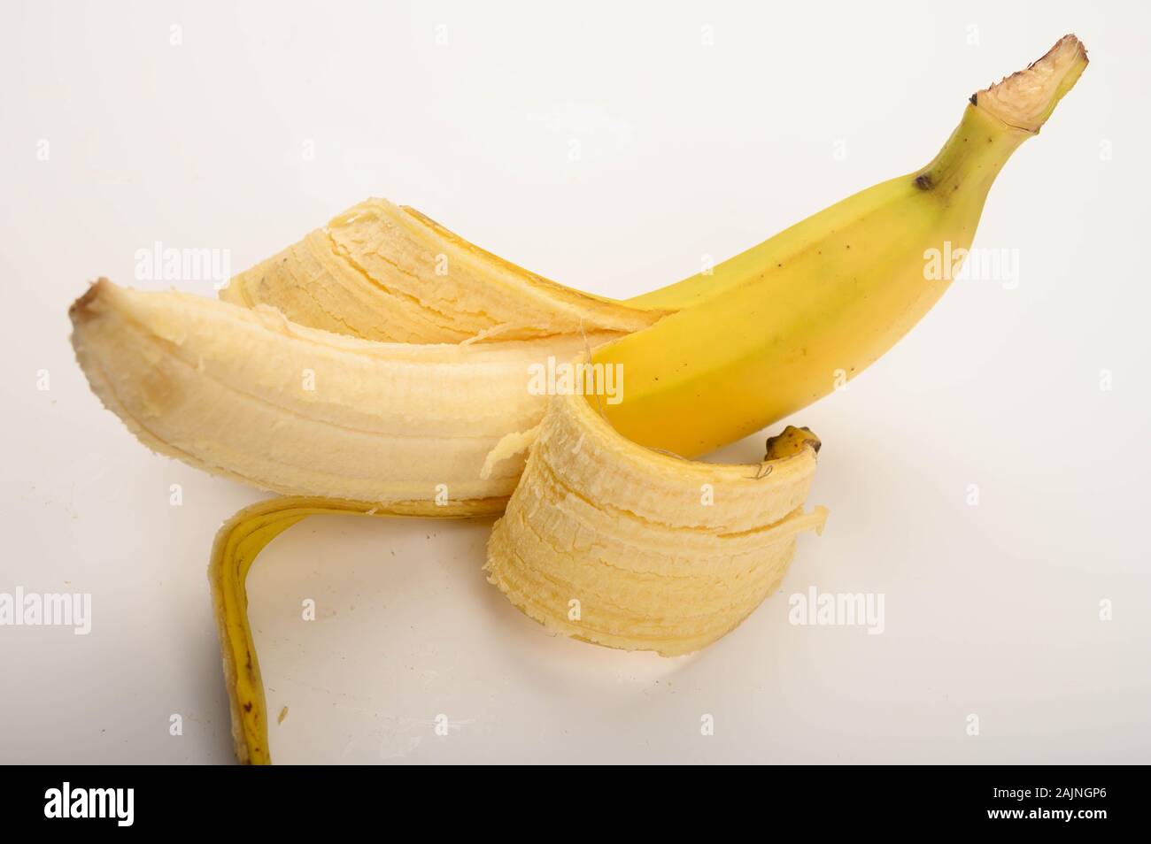 One ripe yellow partially peeled banana on a white background. Close up ...