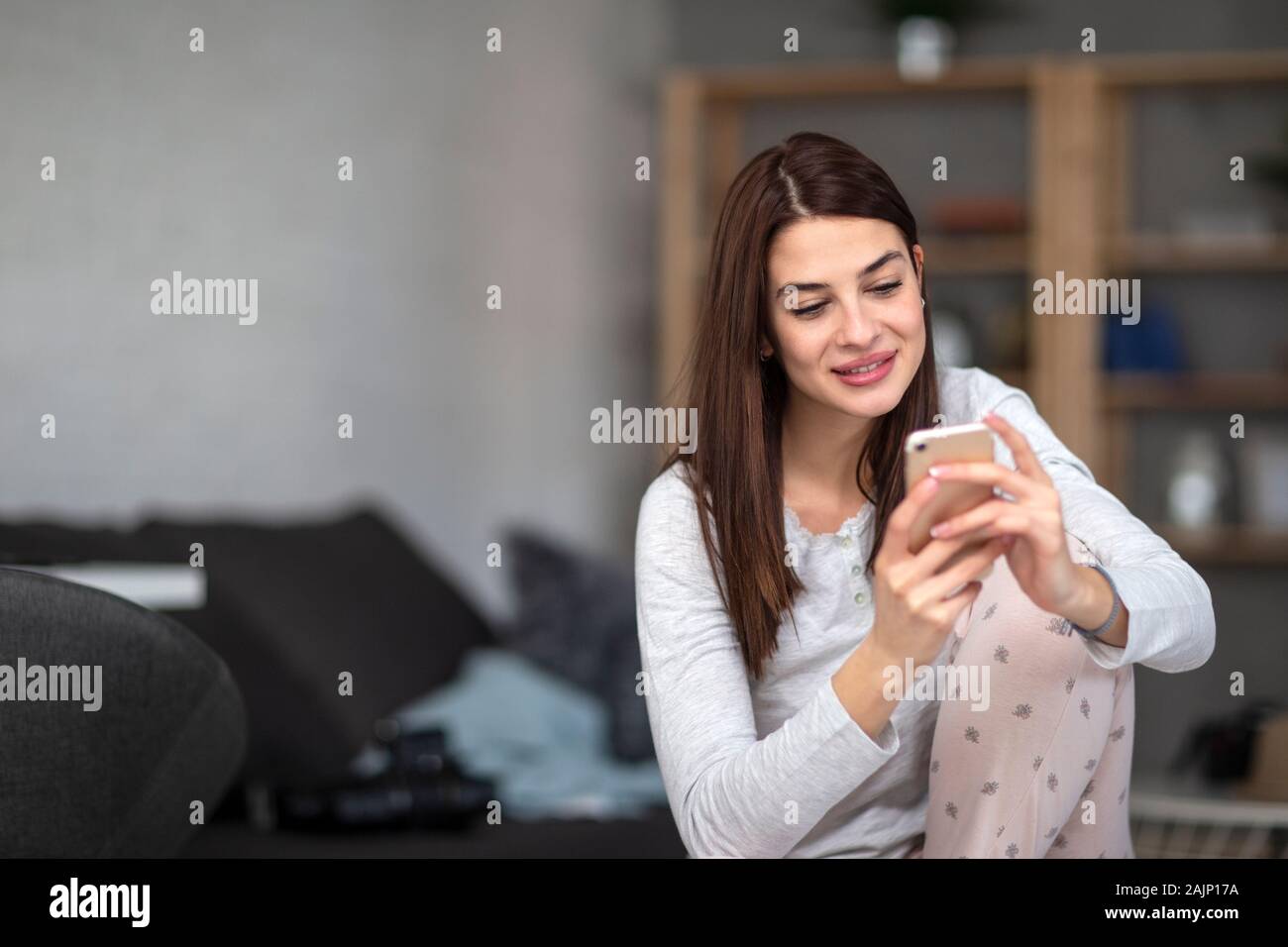 Beautiful young girl in pijama in living room use mobile phone and ...