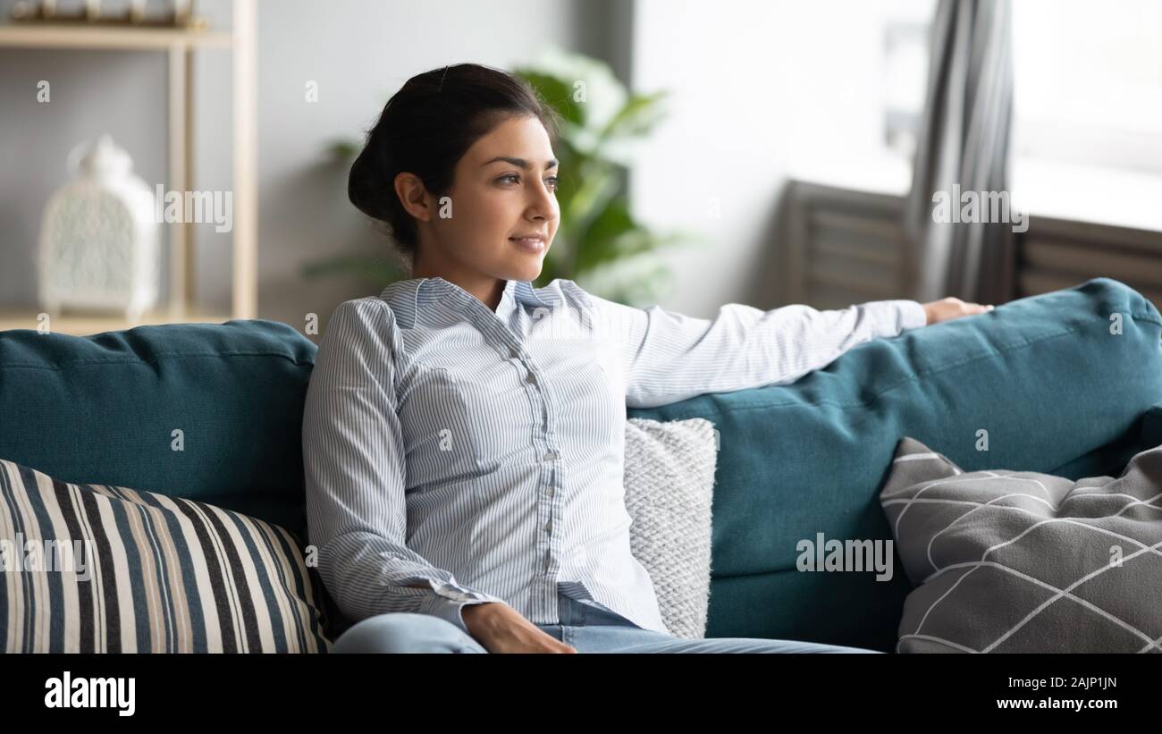 Calm indian lady relaxing on comfortable sofa thinking of wellbeing ...