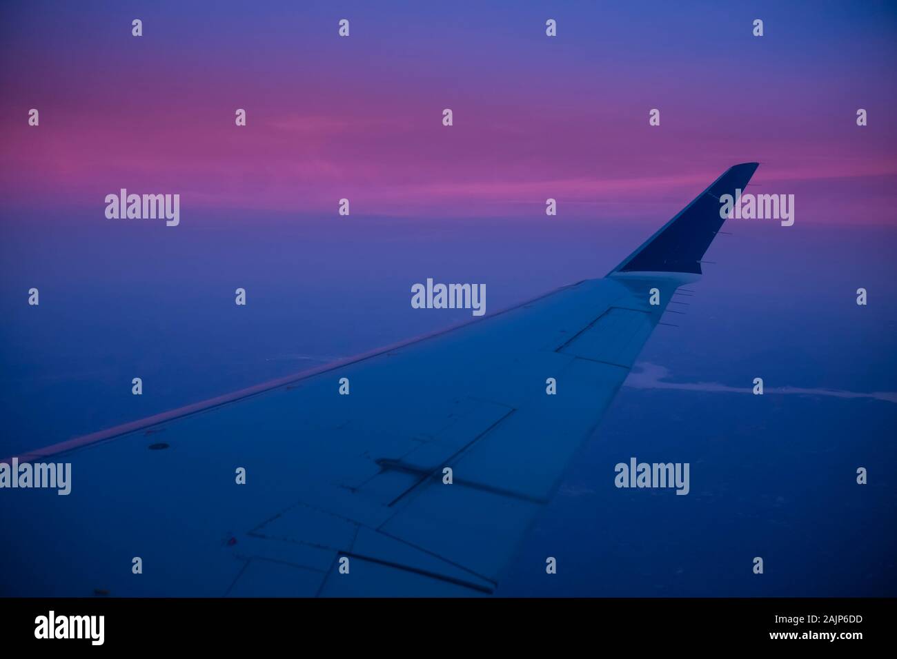 The wing of an airplane is illuminated by the glow of a sunrise along a ...