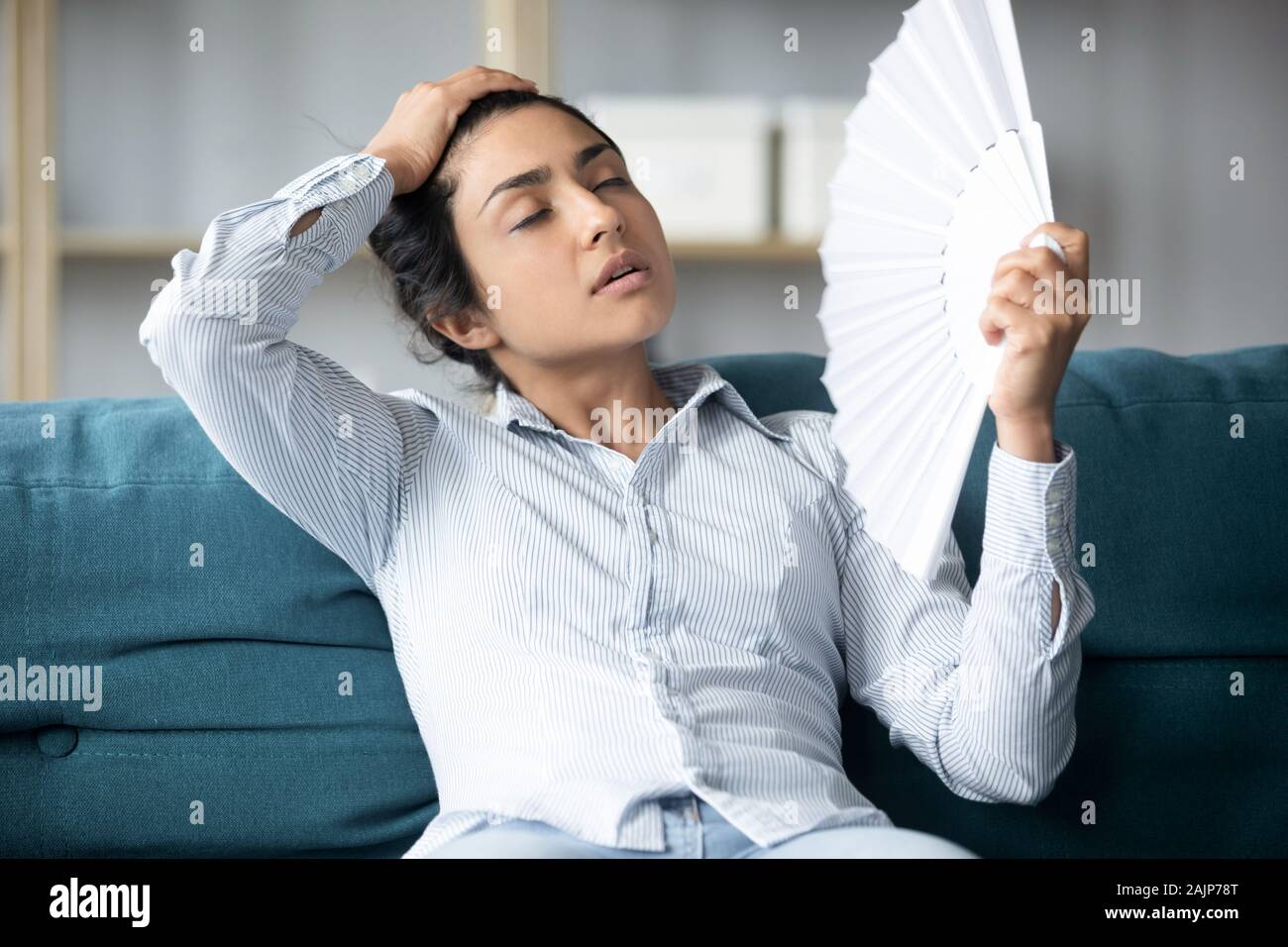 Tired indian woman using fan sit on couch at home Stock Photo - Alamy