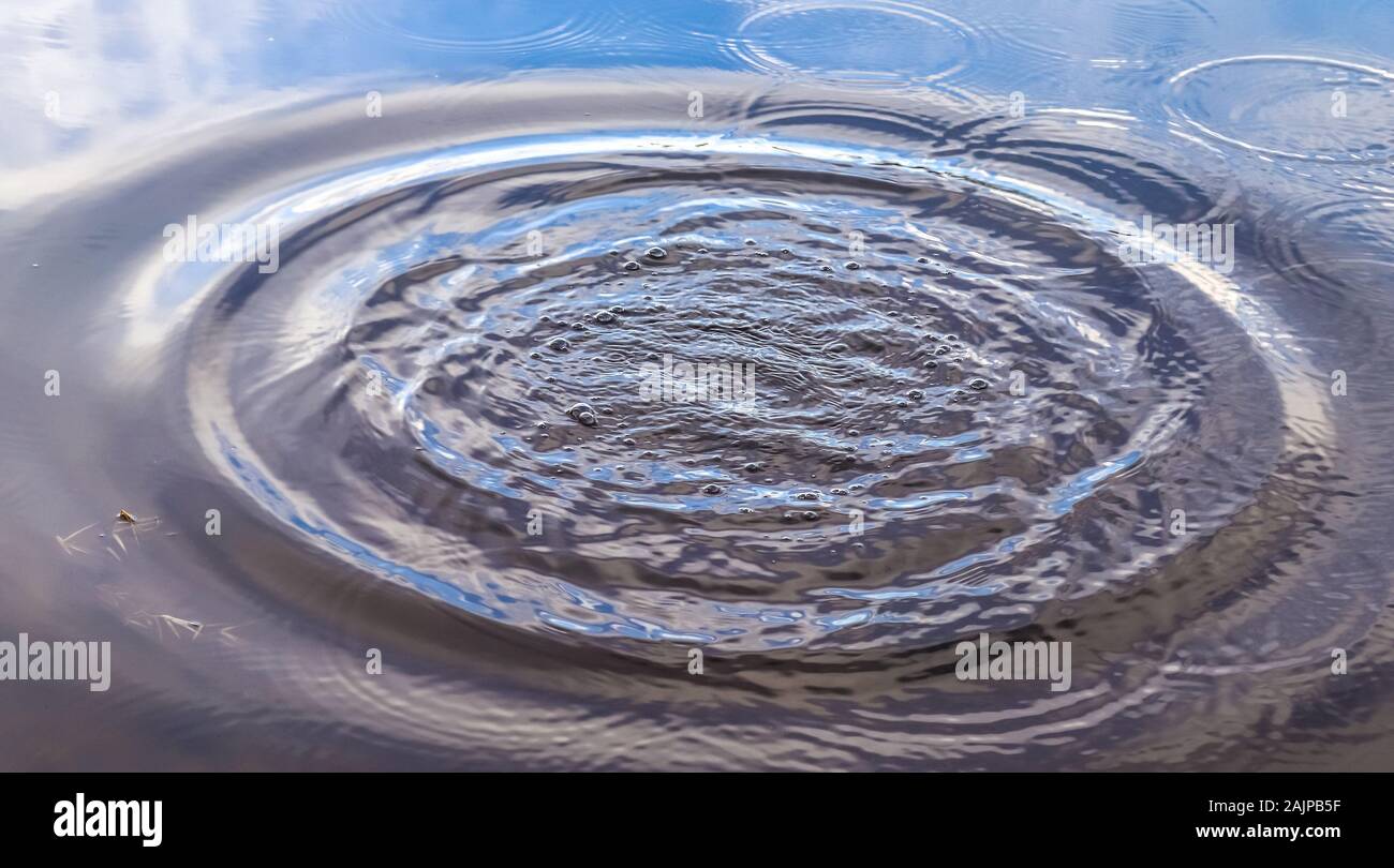 Water splashes and ripples on a water surface with a reflecting blue ...