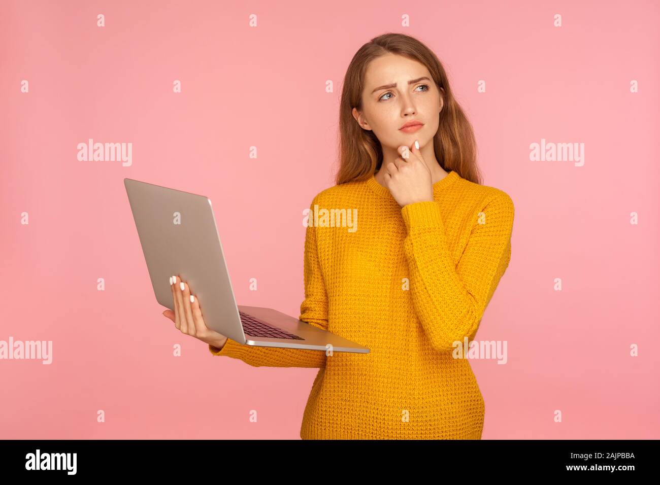 Portrait of thoughtful ginger girl in sweater holding laptop and ...