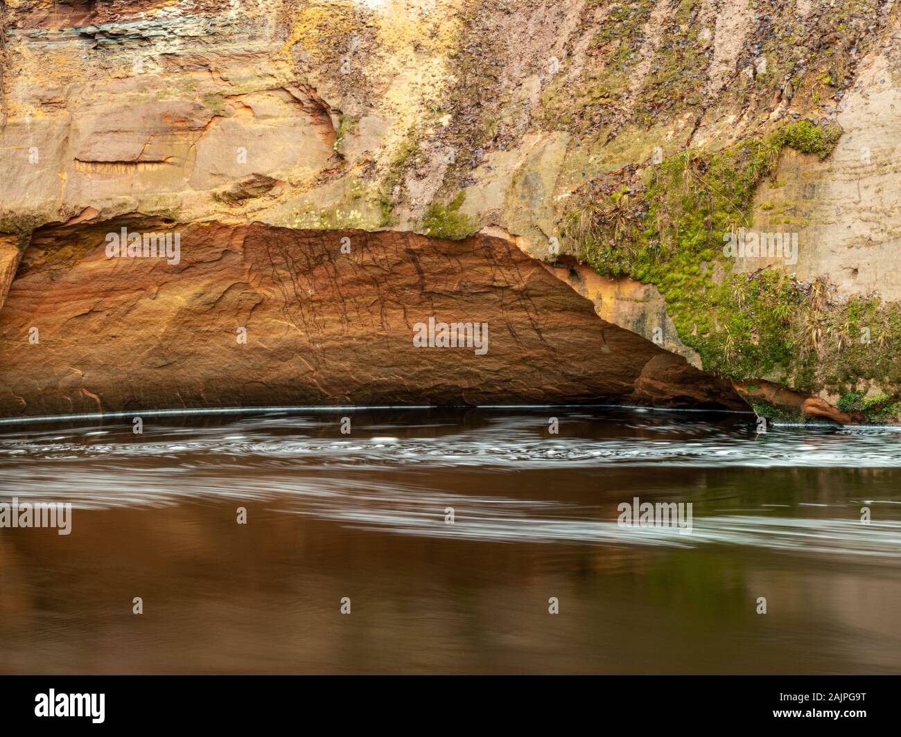 a landscape with a steep river and caves on a sandstone cliff, a cloudy ...