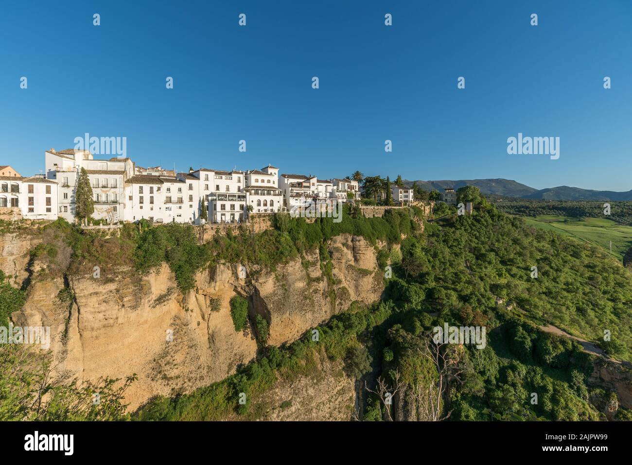 ronda village at the edge of cliffside with trees and white houses ...