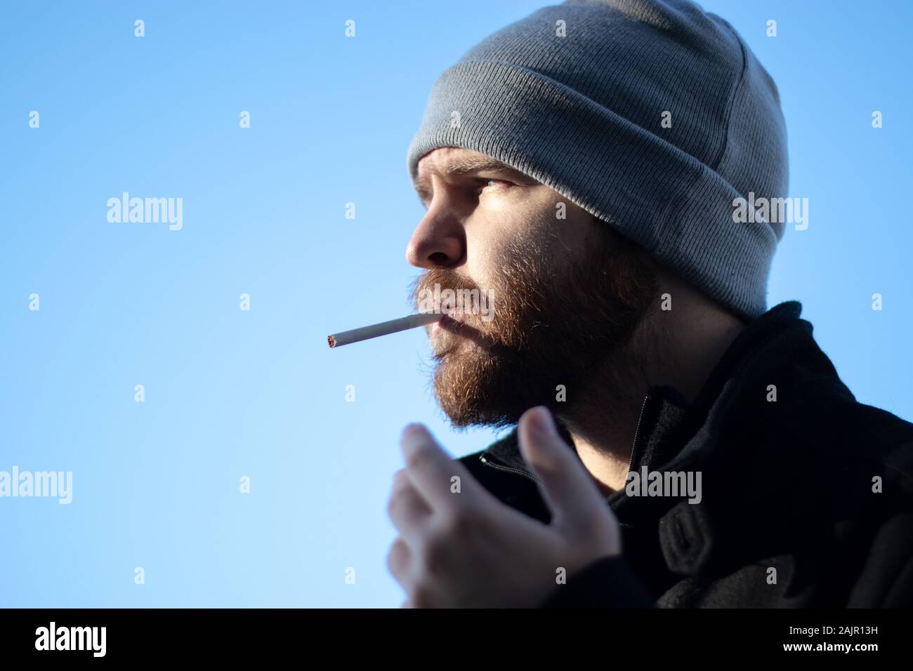 Caucasian bearded male with a beanie holding a cigarette, harshing ...