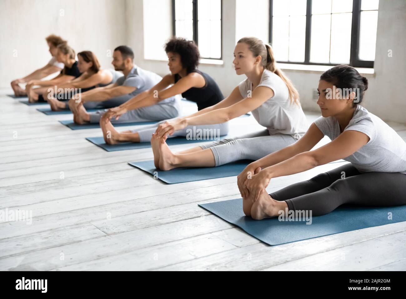 Diverse people sitting in paschimottanasana pose in row, practicing ...