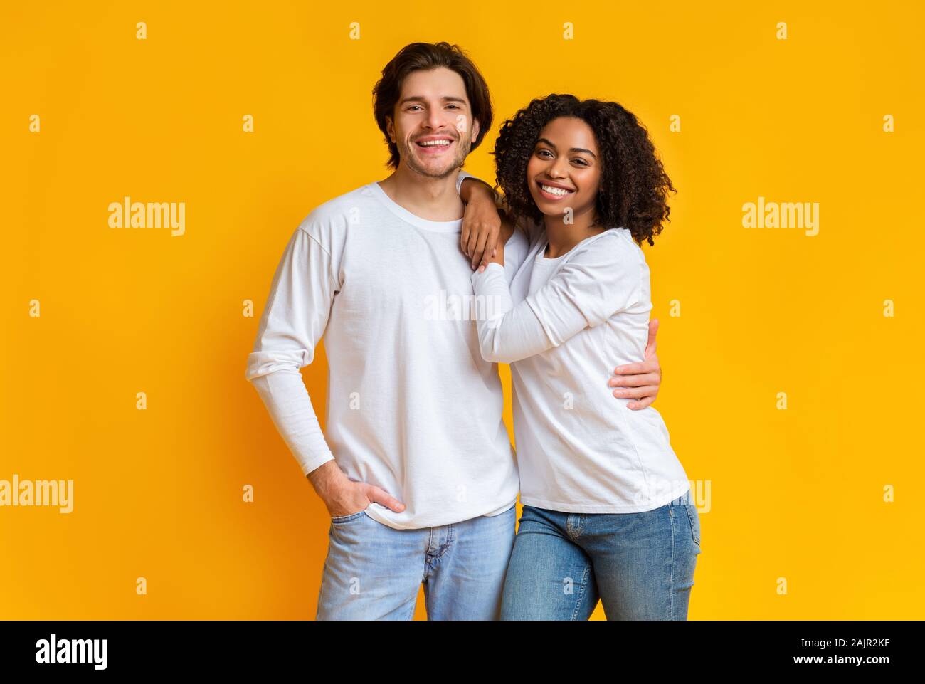 Portrait of smiling mixed-race couple posing over yellow background in ...