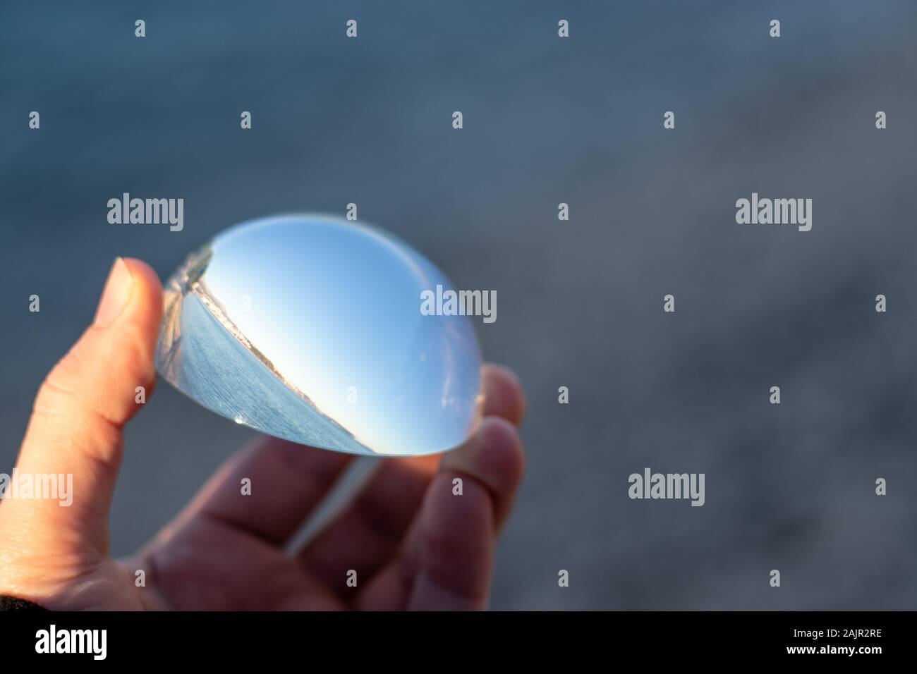 Hand holding a crystal glass hemisphere, blue reflections of ...