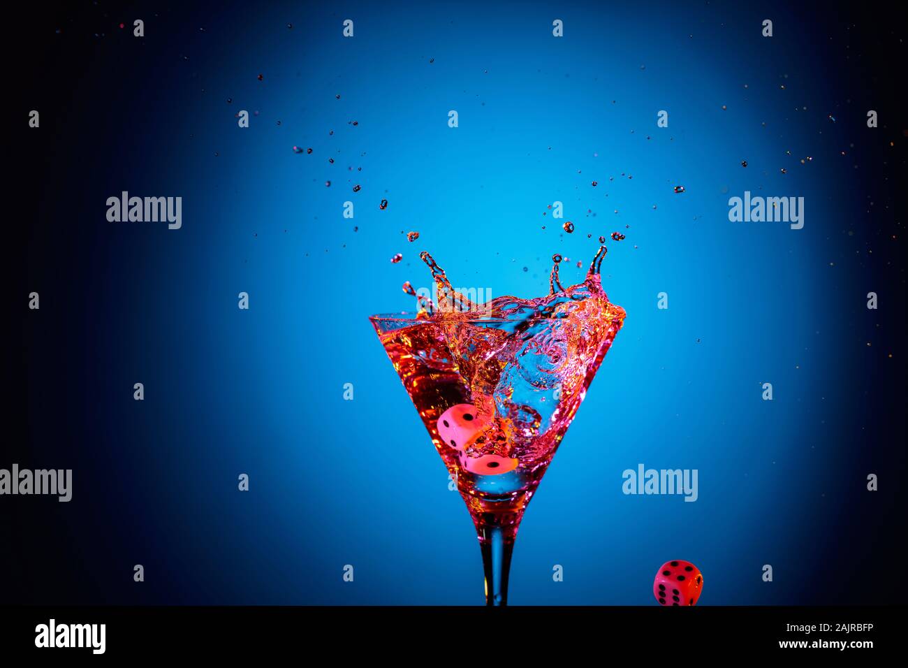 Dice fall in a glass of martini. Colourful cocktail in glass with ...