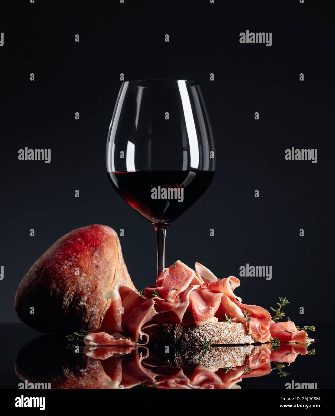 Prosciutto with ciabatta, red wine and thyme on a black reflective ...