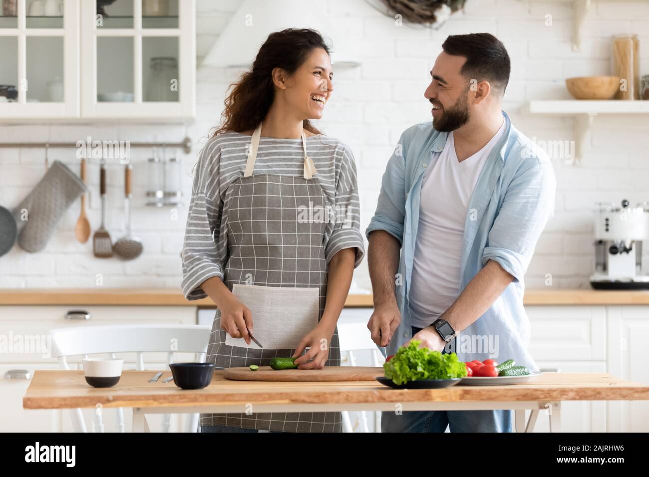 Spouses preparing salad standing on cozy kitchen enjoy cooking process ...