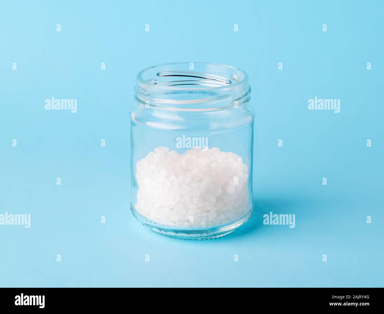 Large white crystals of sea salt in a glass bottle on a pastel blue ...
