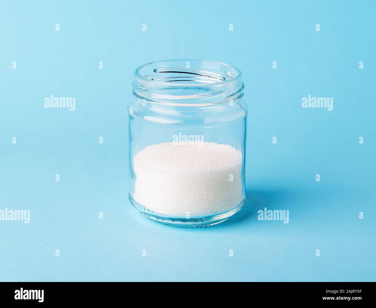 White crystals of sugar in a glass bottle on a pastel blue background ...