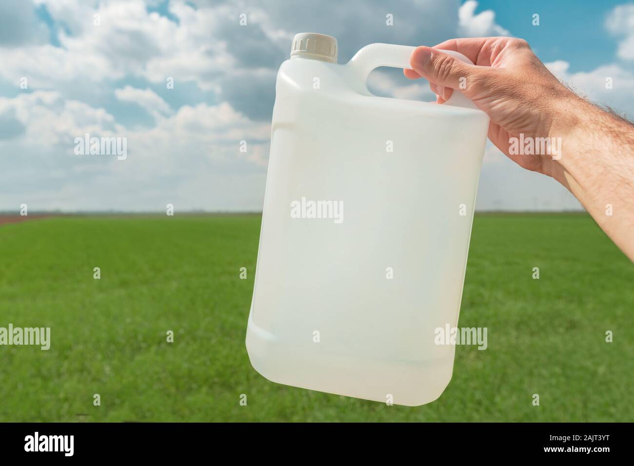 Farmer holding insecticide jug in wheatgrass field, blank plastic ...
