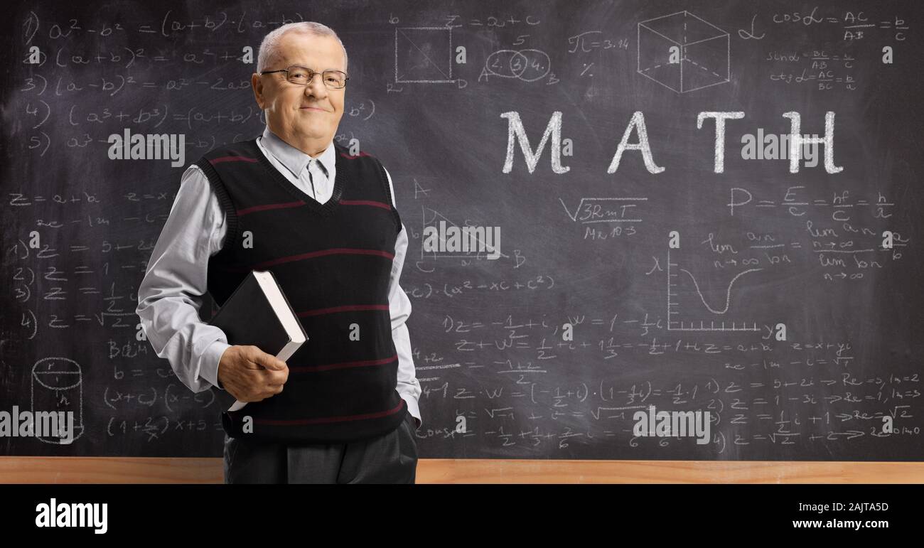 Mature math teacher with a book in front of a blackboard with formulas ...