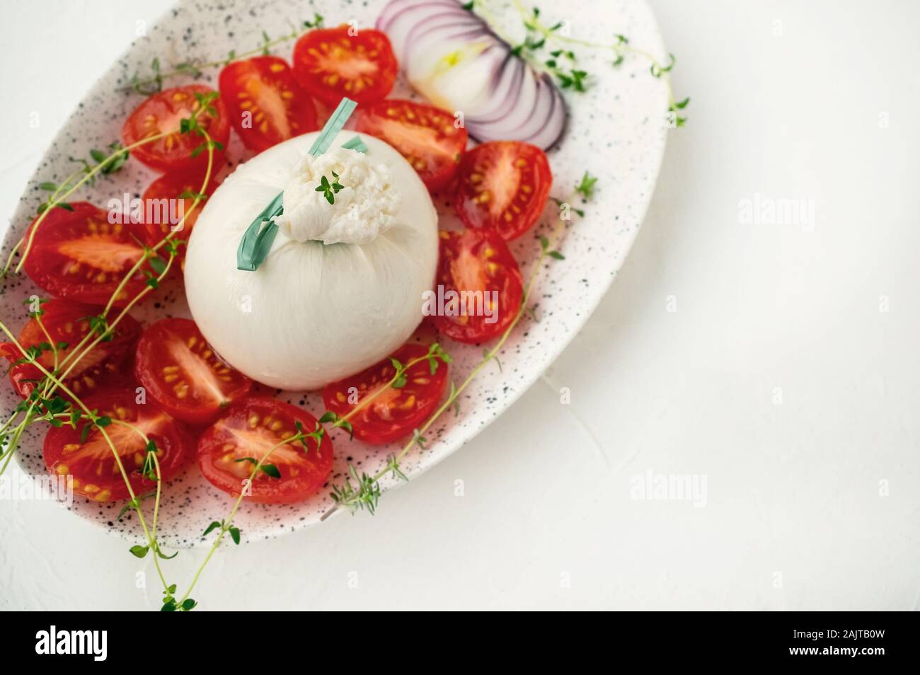 Fresh Italian burrata cheese with tomato slices on a light plate on a ...