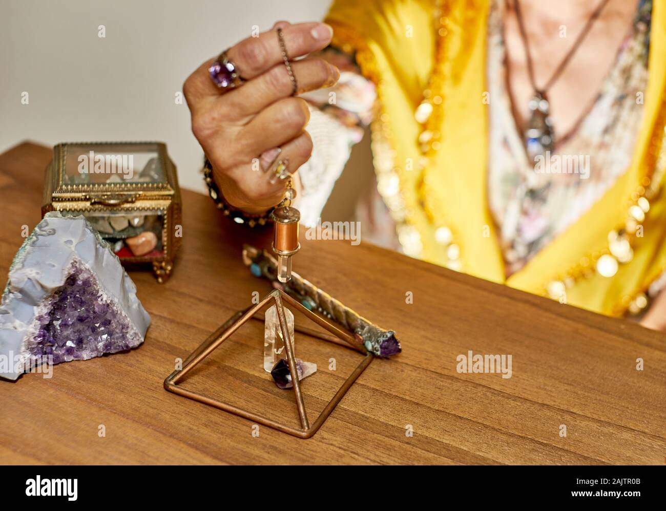 A spiritual healer using a crystal pendulum over another quartz crystal ...