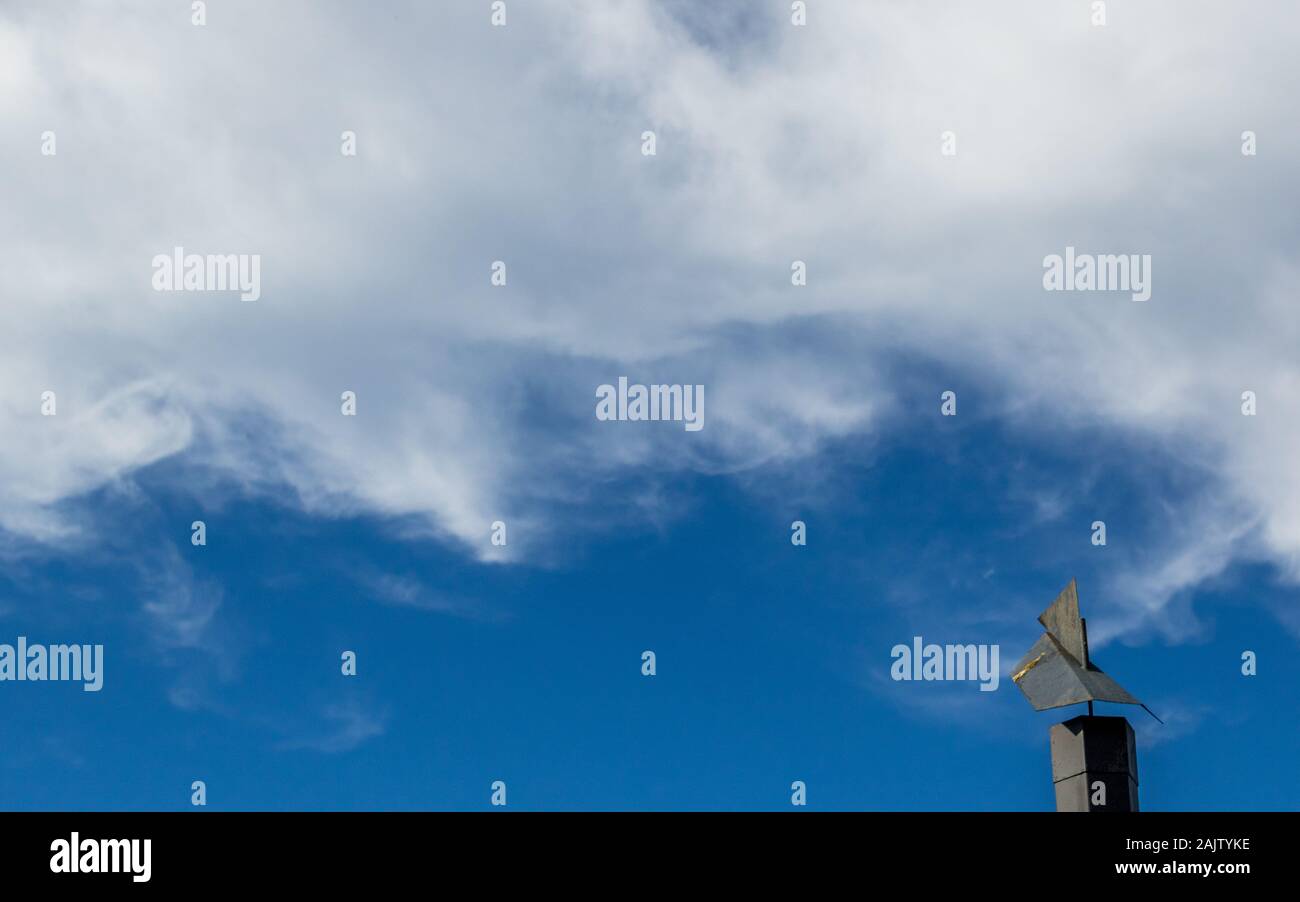 Top of a black chimney with a weather vane isolated against a blue sky ...