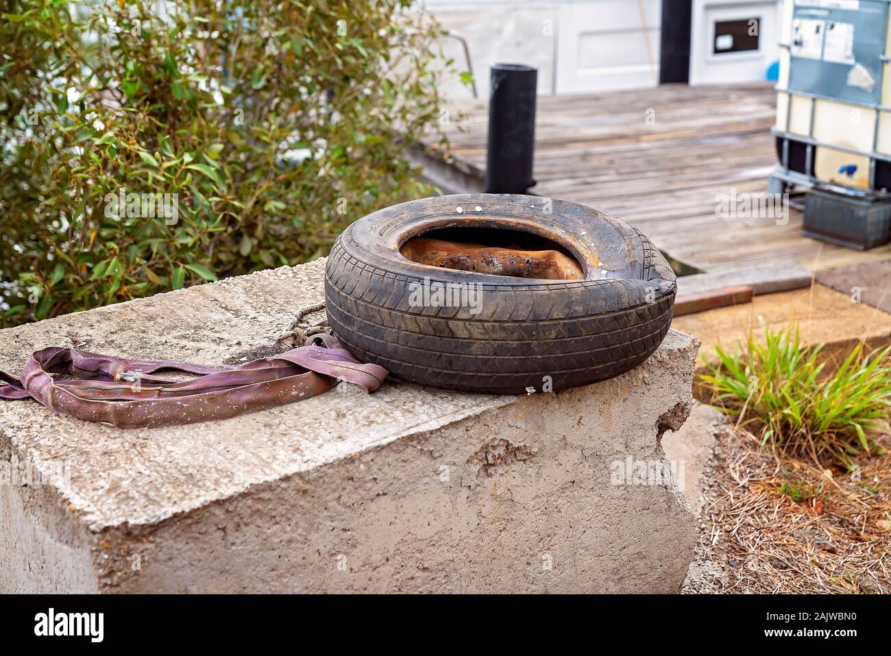 An old flat tyre with rusted rim discarded outside on a concrete post ...