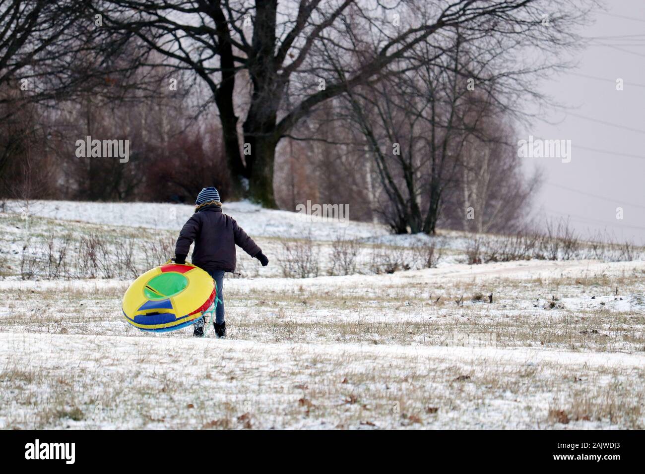 Child having fun on snow tube in a park, boy sliding down the hill ...