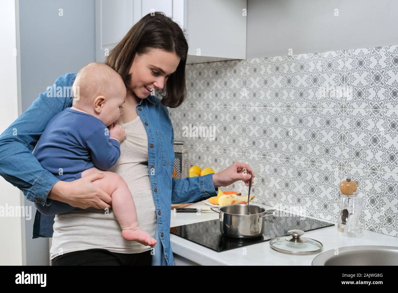 Young beautiful woman with baby in her arms in kitchen Stock Photo - Alamy