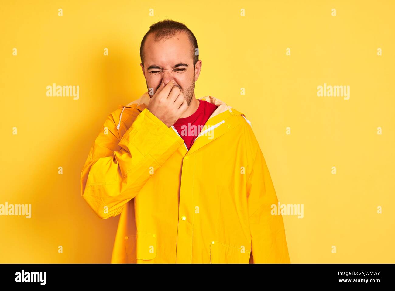 Young man wearing rain coat standing over isolated yellow background ...