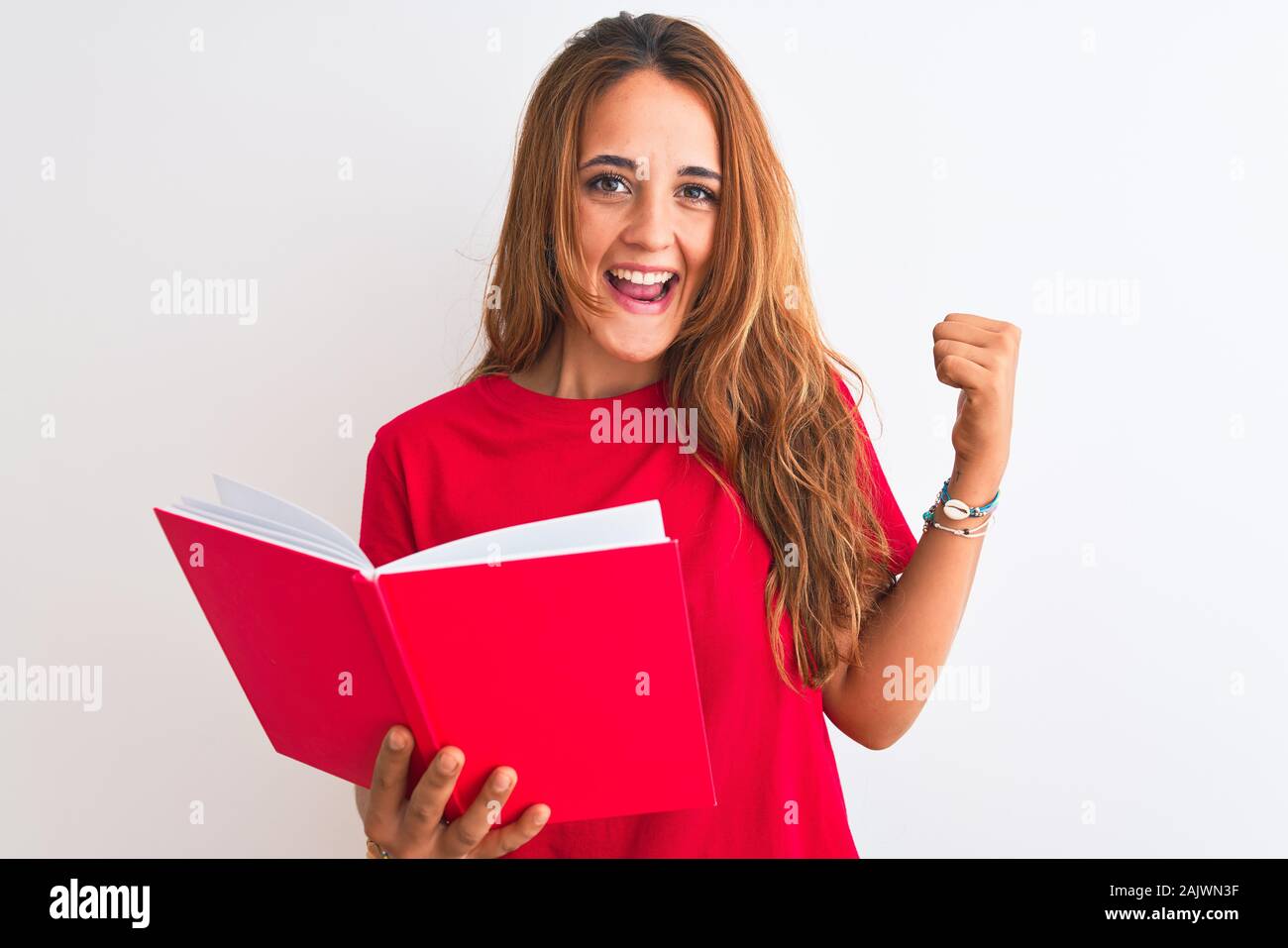 Young beautiful redhead woman reading a red book over isolated ...