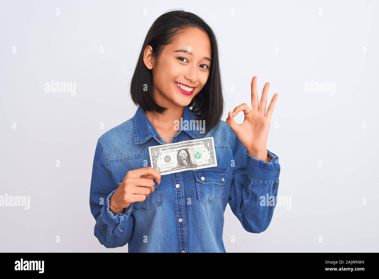 Young beautiful chinese woman holding one dollar standing over isolated ...
