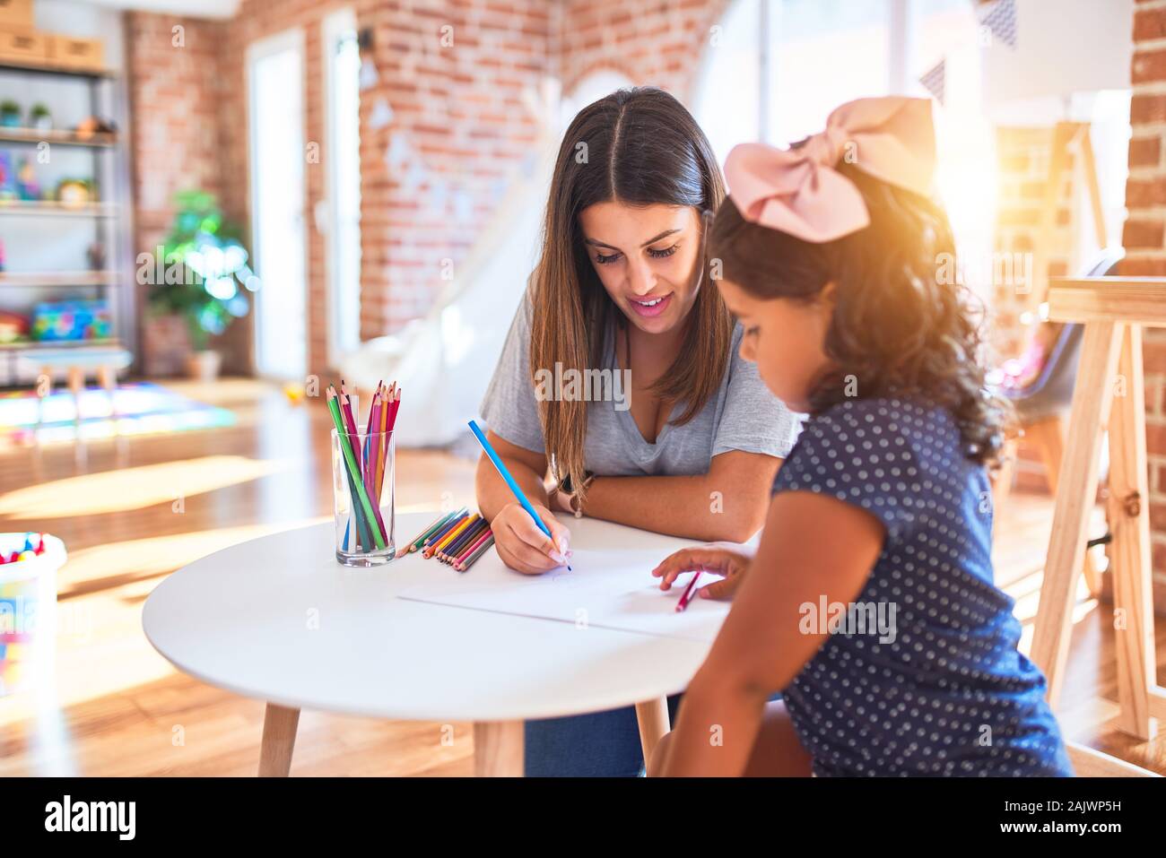 Beautiful teacher and toddler girl drawing draw using colored pencils ...