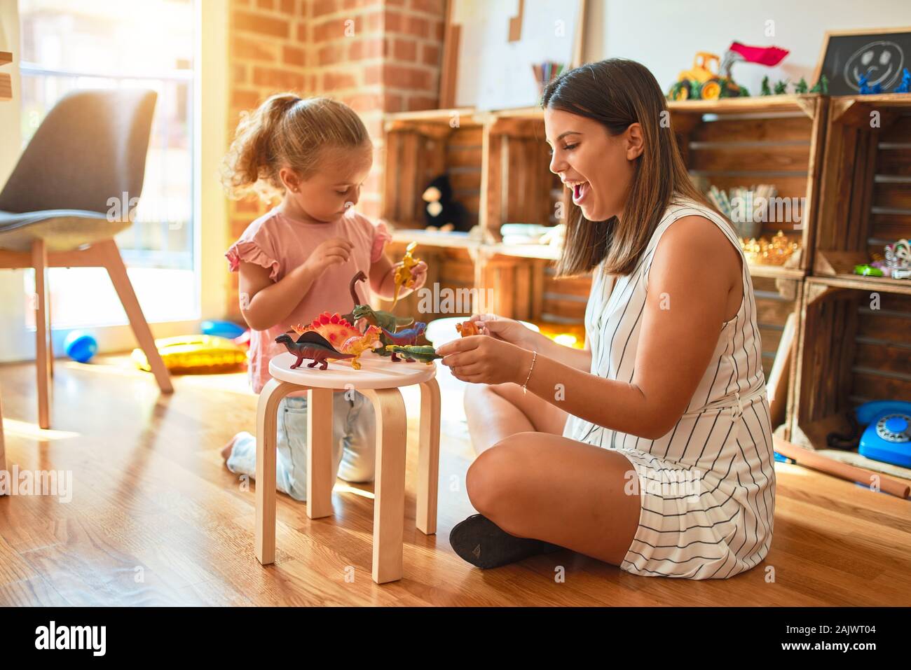 Beautiful teacher and blond student toddler girl playing with dinosaurs ...