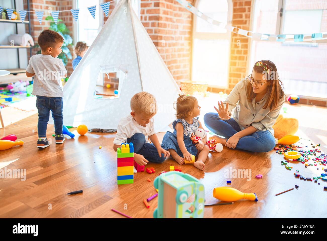 Beautiful teacher and group of toddlers playing around lots of toys at ...
