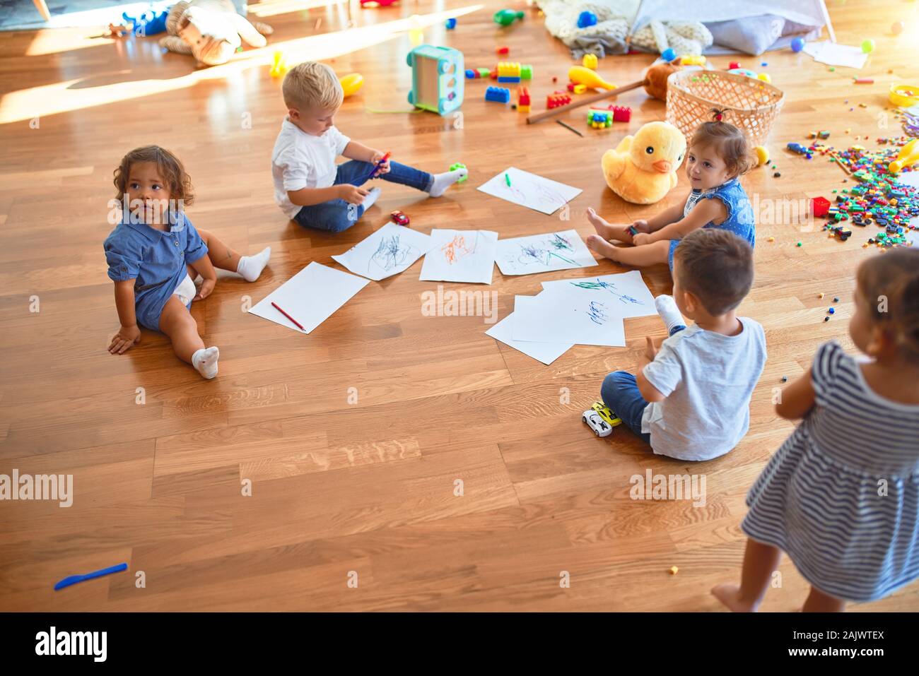 Adorable group of toddlers sitting on the floor drawing using paper and ...