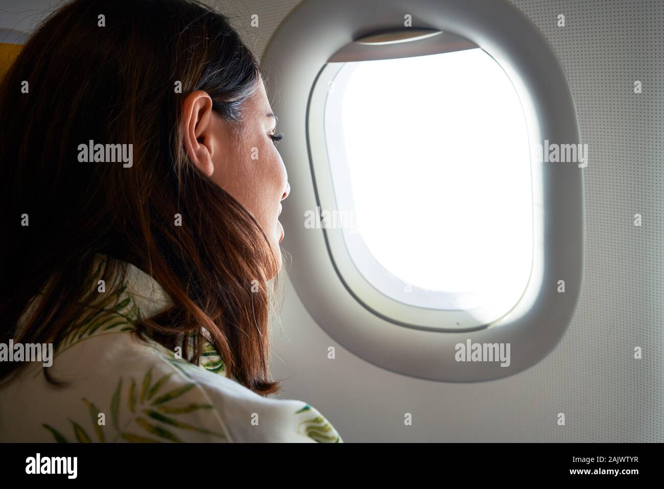 Young traveller woman sitting inside plane at the airport with sky view ...