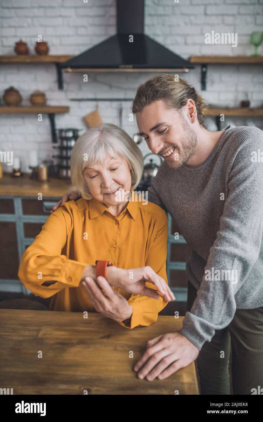 Good-looking elderly lady in yellow putting on smartwatch Stock Photo ...