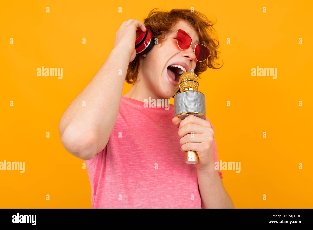 red-haired teenager singer in headphones sings on a yellow background ...