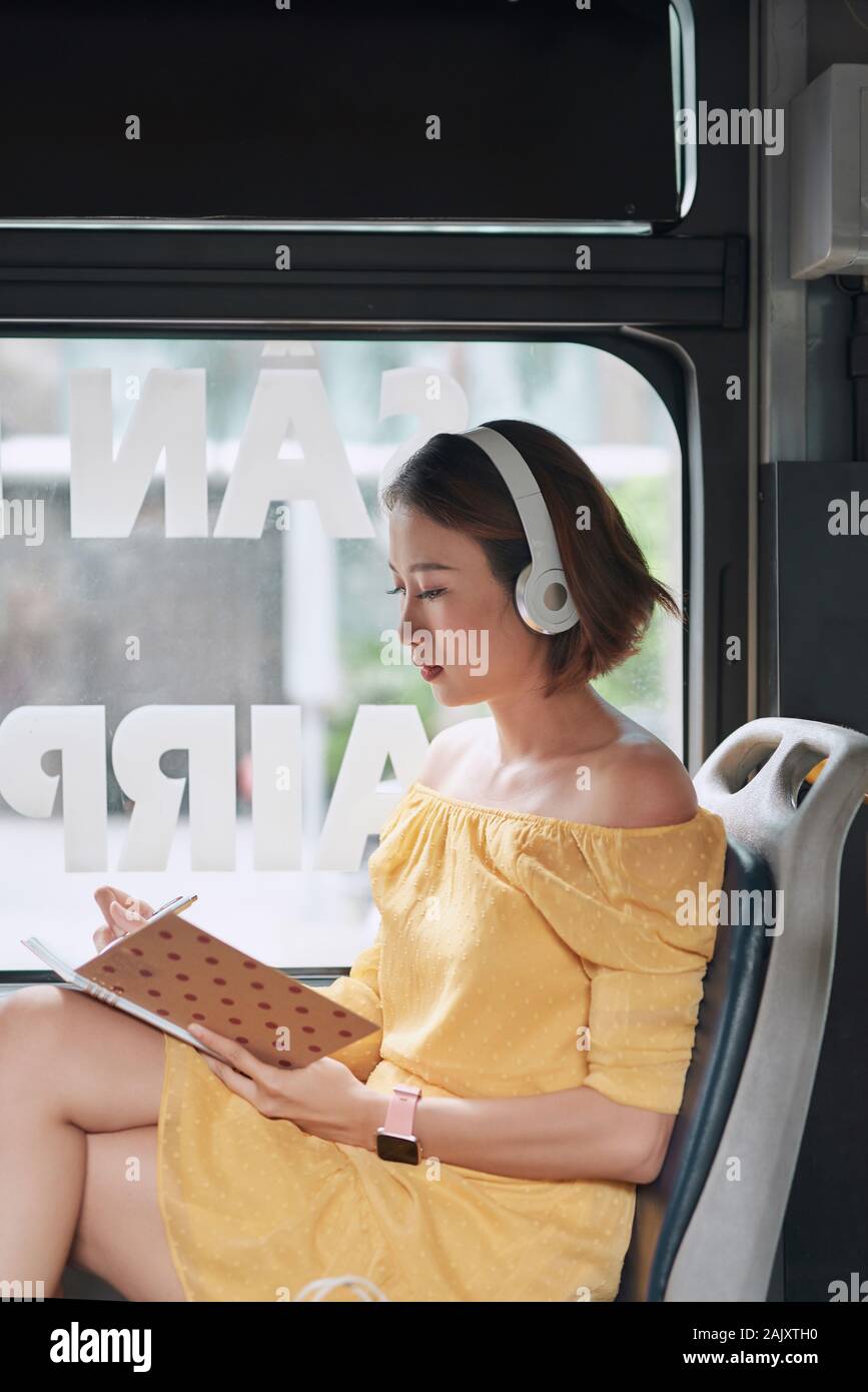 Beautiful young woman sitting in city bus and writing some notes in ...
