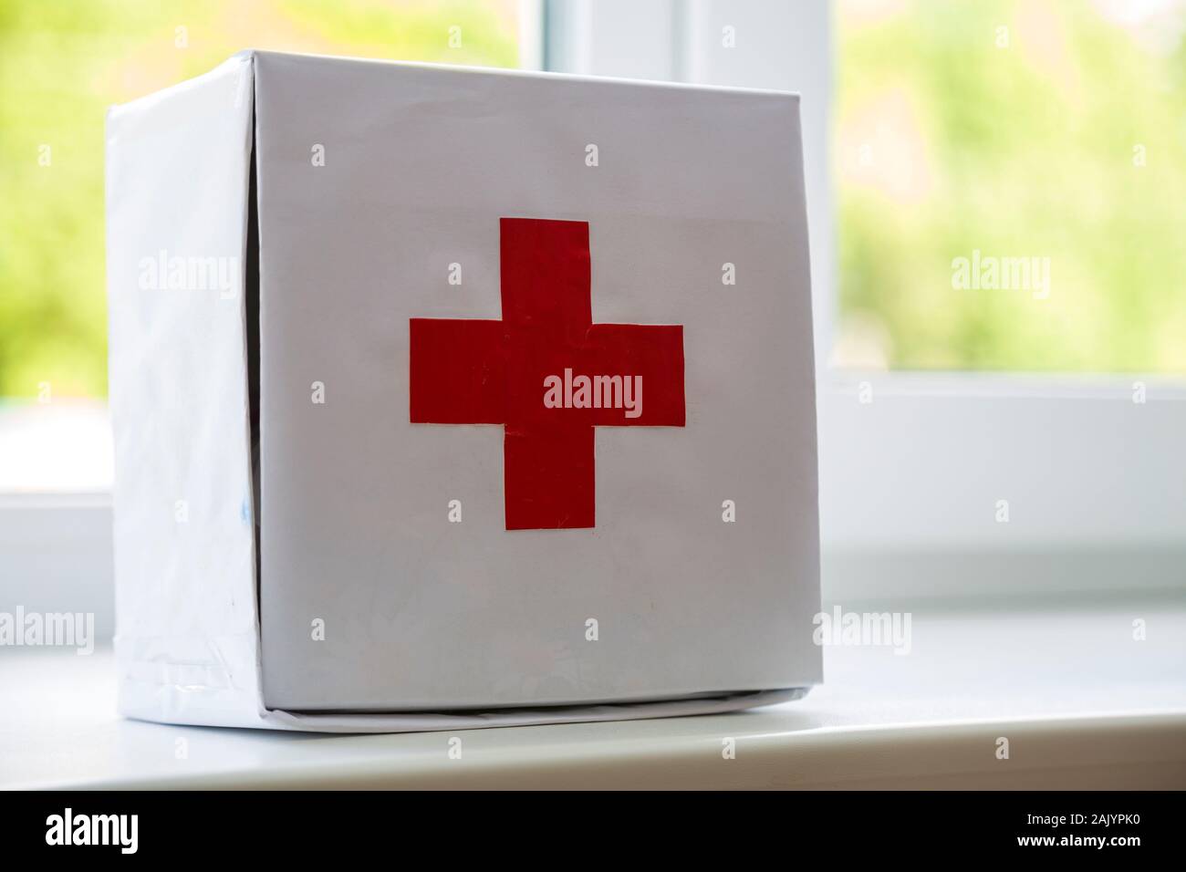 White first aid kit with red cross indoors on windowsill on blurred ...