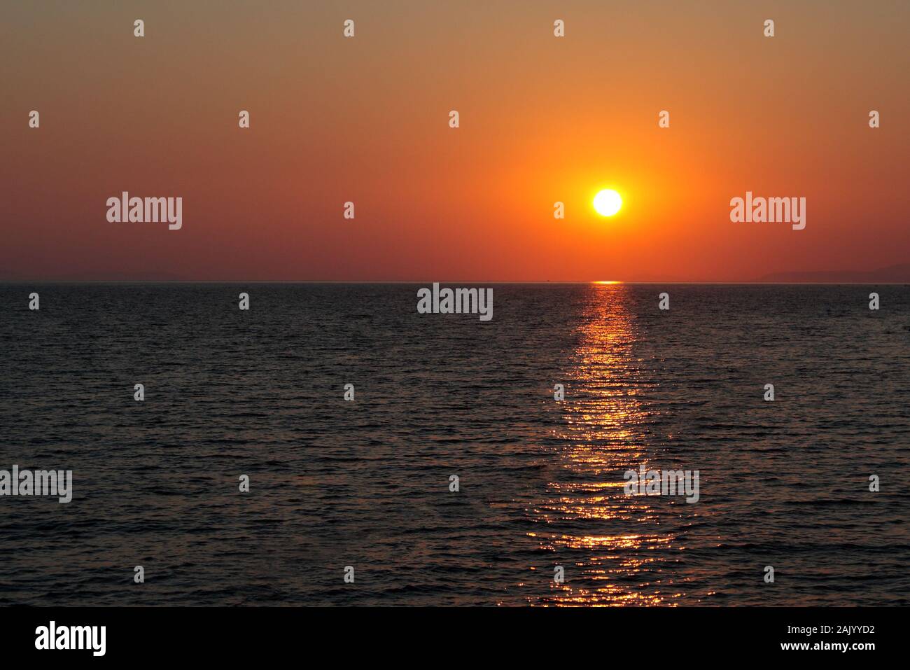 Setting sun over the sea, clear (reddish) sky Stock Photo - Alamy