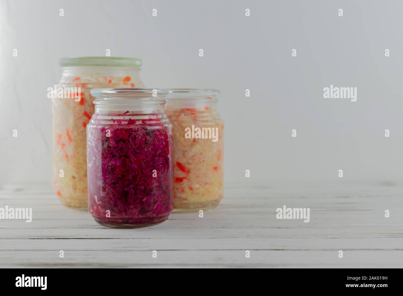 three glass jars of fermented white, red cabbage. vegetables on a light ...