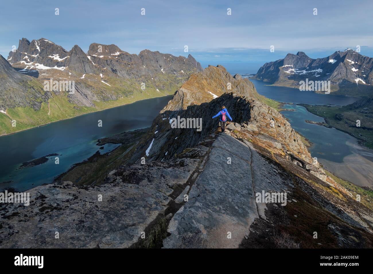 Female hiker descending rocky narrow ridge from Helvetestind mountain ...