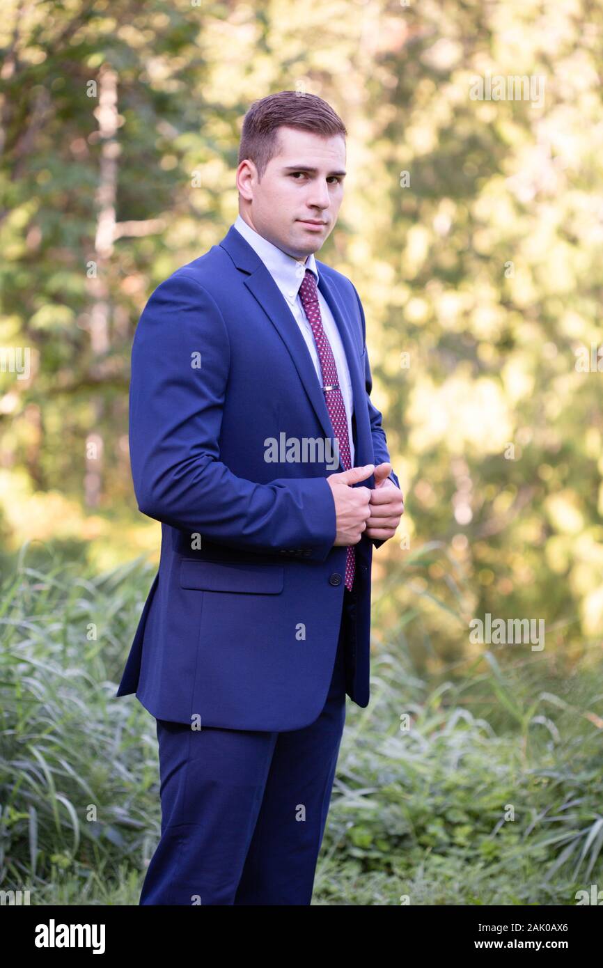 Confident young man in suit stands in front of trees Stock Photo - Alamy